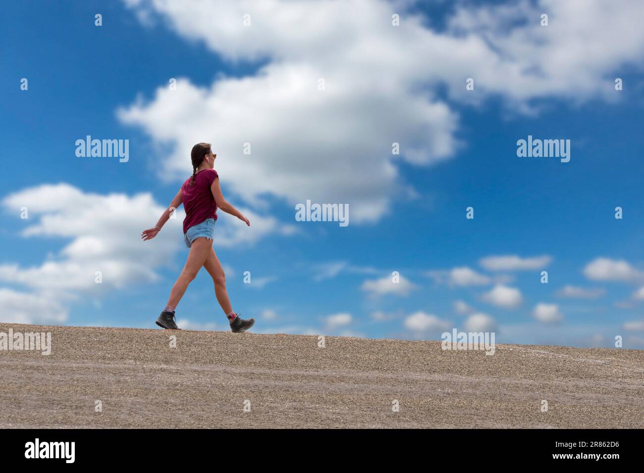 Young woman / girl walking at a fast pace against blue cloudy sky with ...