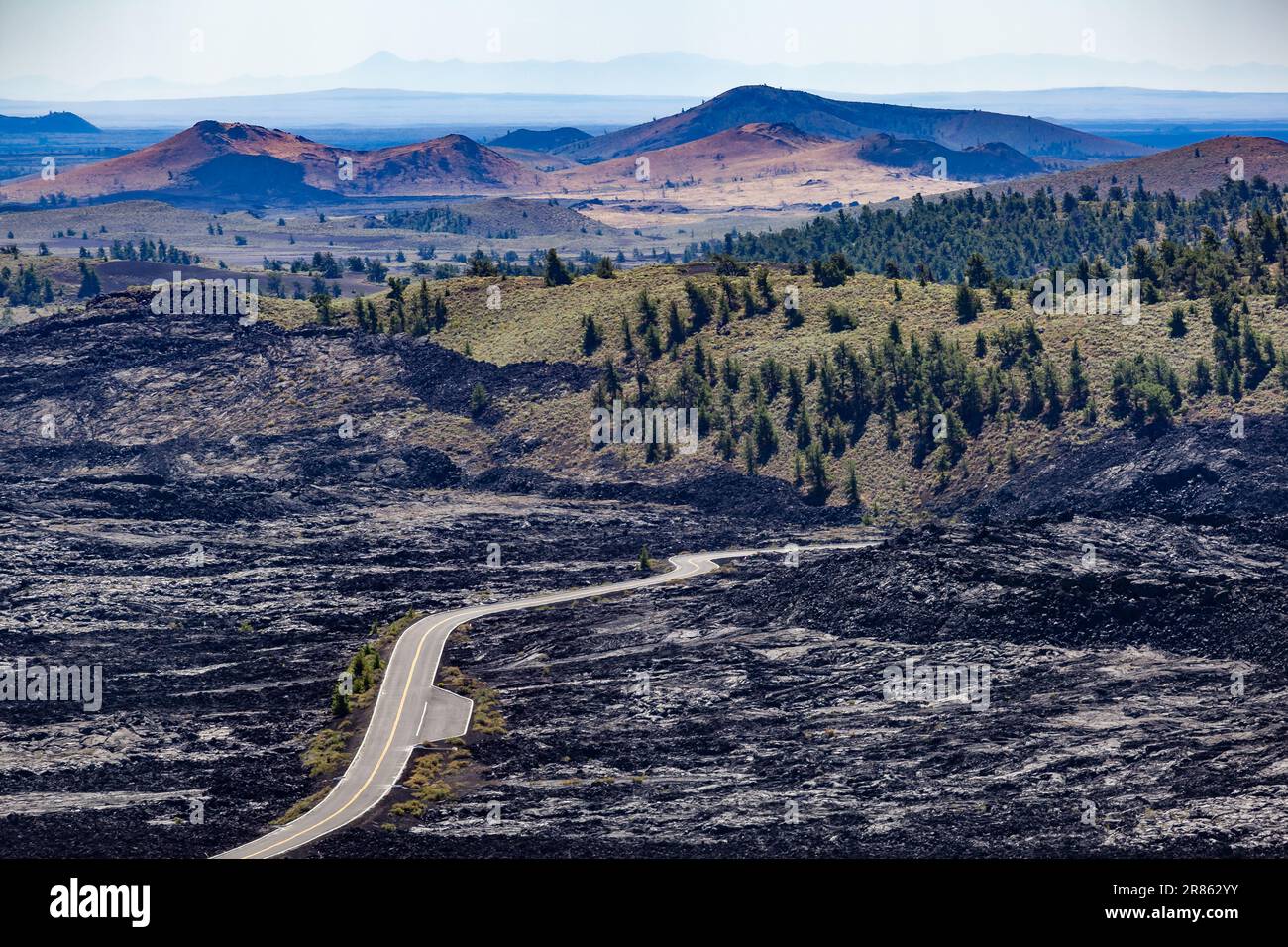 Road that runs between lava rocks and grasslands with pine trees ...