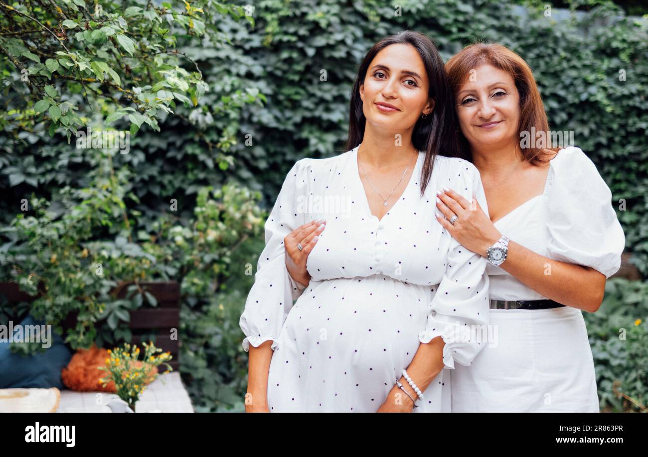 Attractive pregnant brunette has her mom cuddling outdoors in the ...