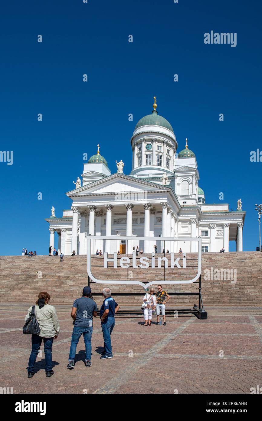 Tourists posing in front of Helsinki logo sign and Helsinki Cathedral ...