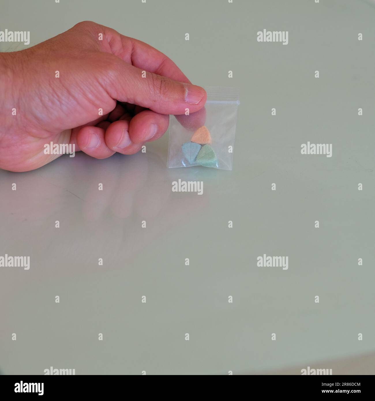 Hand holding a baggie with Tesla ecstasy pills in orange, green, and ...