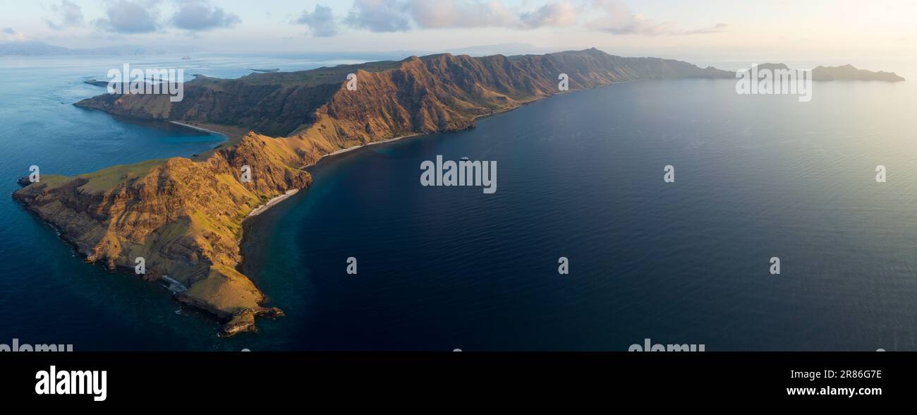 Evening sunlight illuminates the volcanic island of Gili Banta near ...
