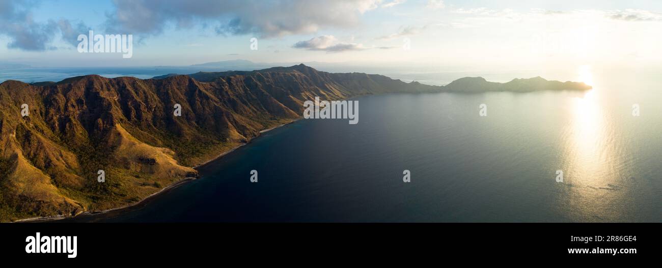 Evening sunlight illuminates the volcanic island of Gili Banta near ...