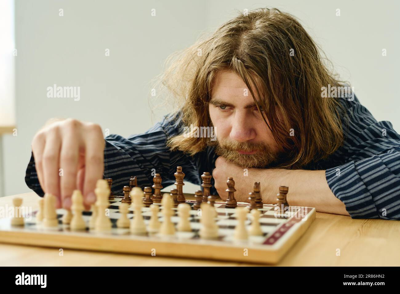 Young depressed man with beard and long hair playing chess on his own ...