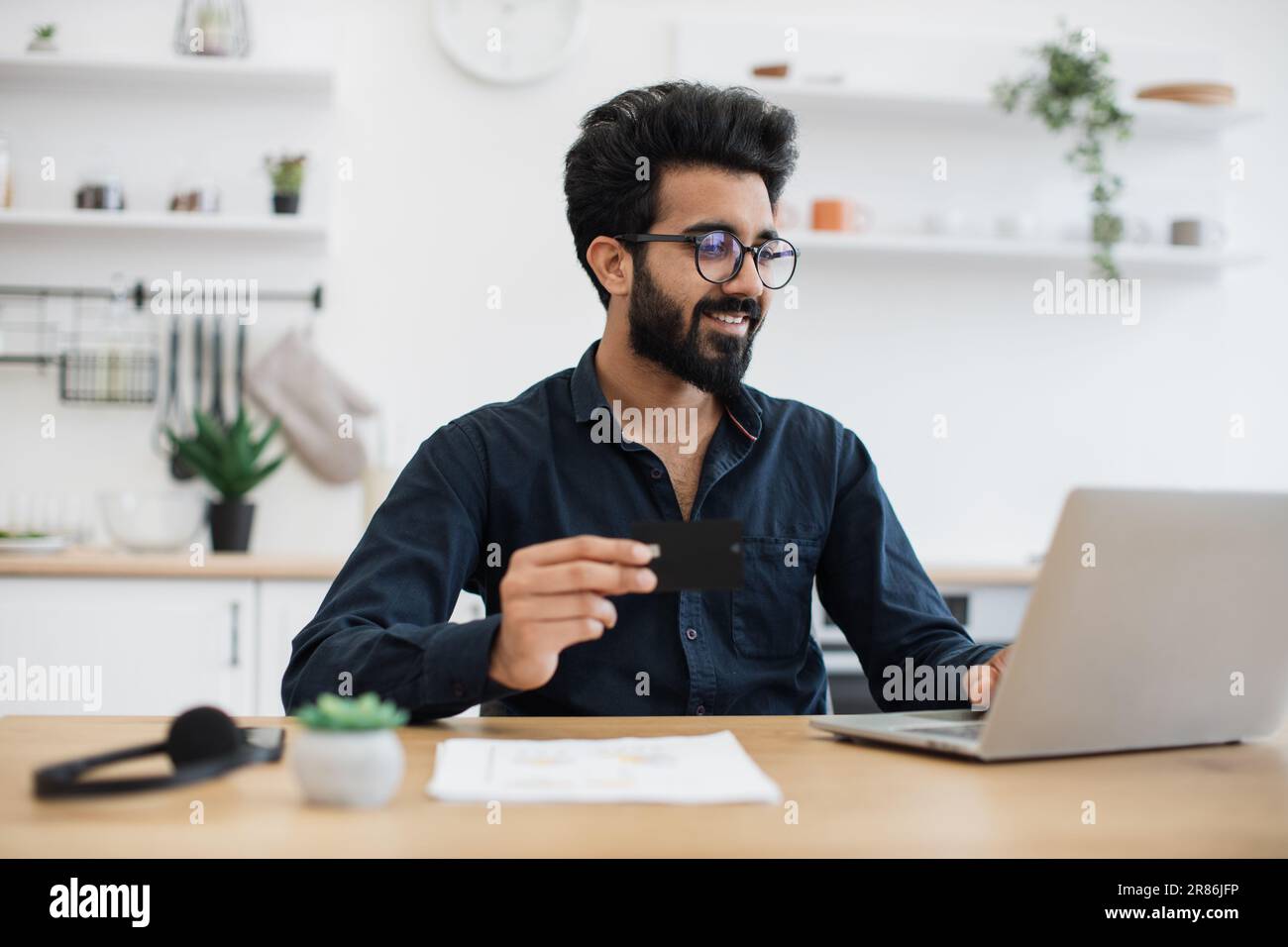 Attractive bearded man in spectacles holding blank credit card while ...