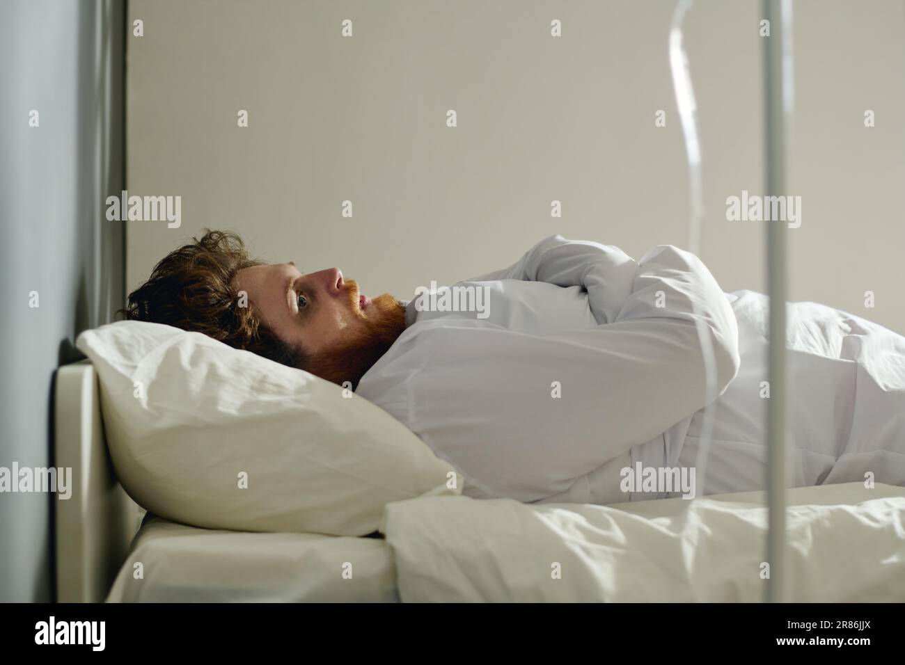 Side view of young male patient in straitjacket lying on bed in ward of ...
