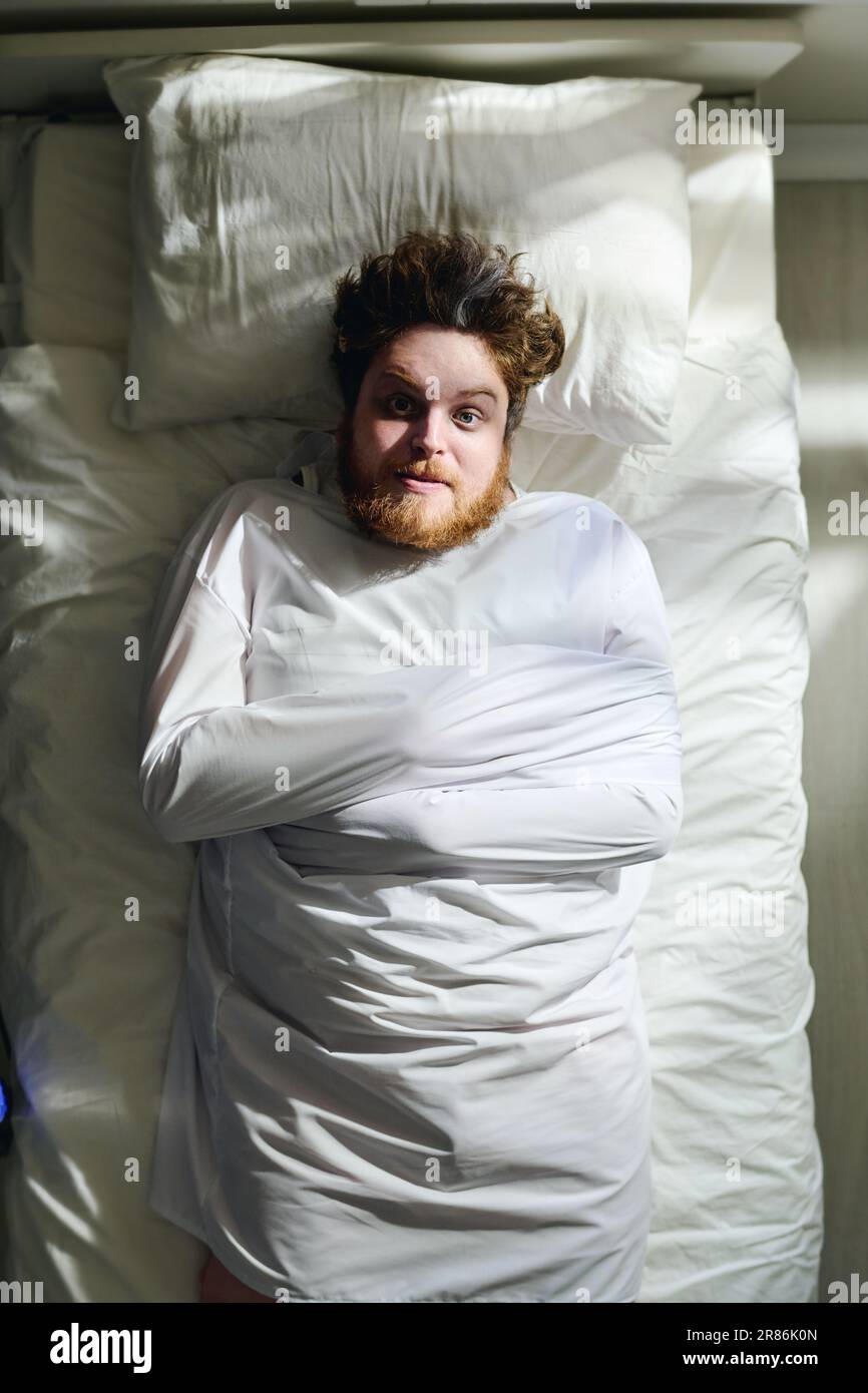 Above view of young insane male patient in straitjacket looking at ...