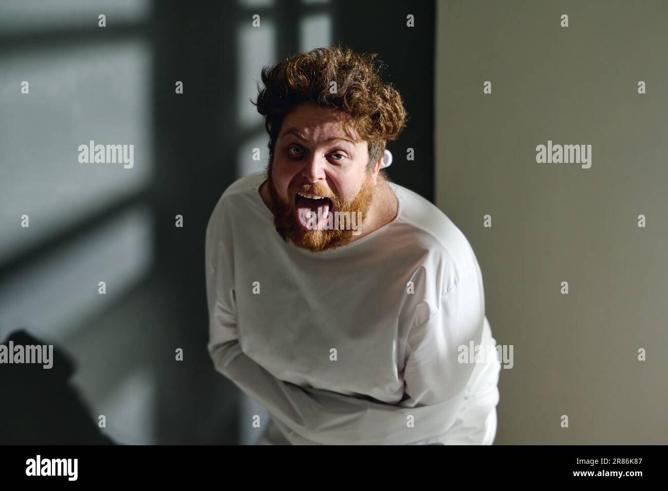 Young insane man in straitjacket showing tongue and screaming while ...