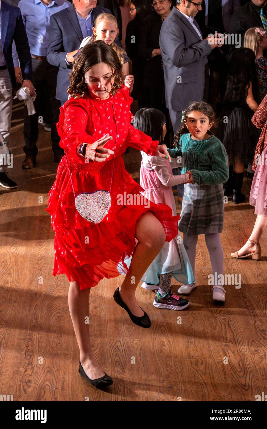 A young Hispanic girl looks in amazement at an older girl dancing alone ...