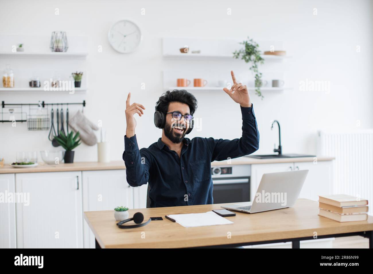 Excited young man moving hands high in air to melody while sitting with ...