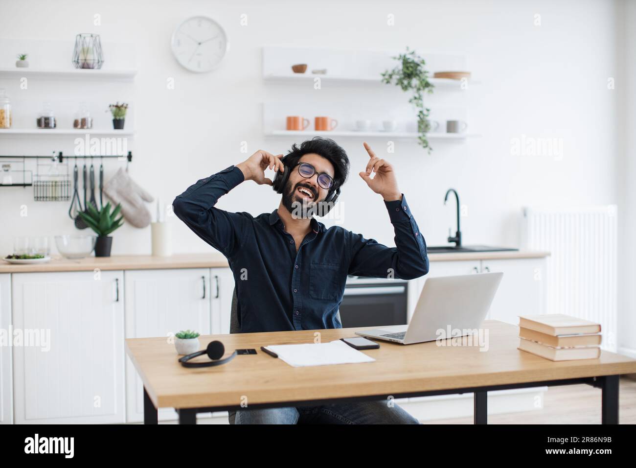 Excited young man moving hands high in air to melody while sitting with ...