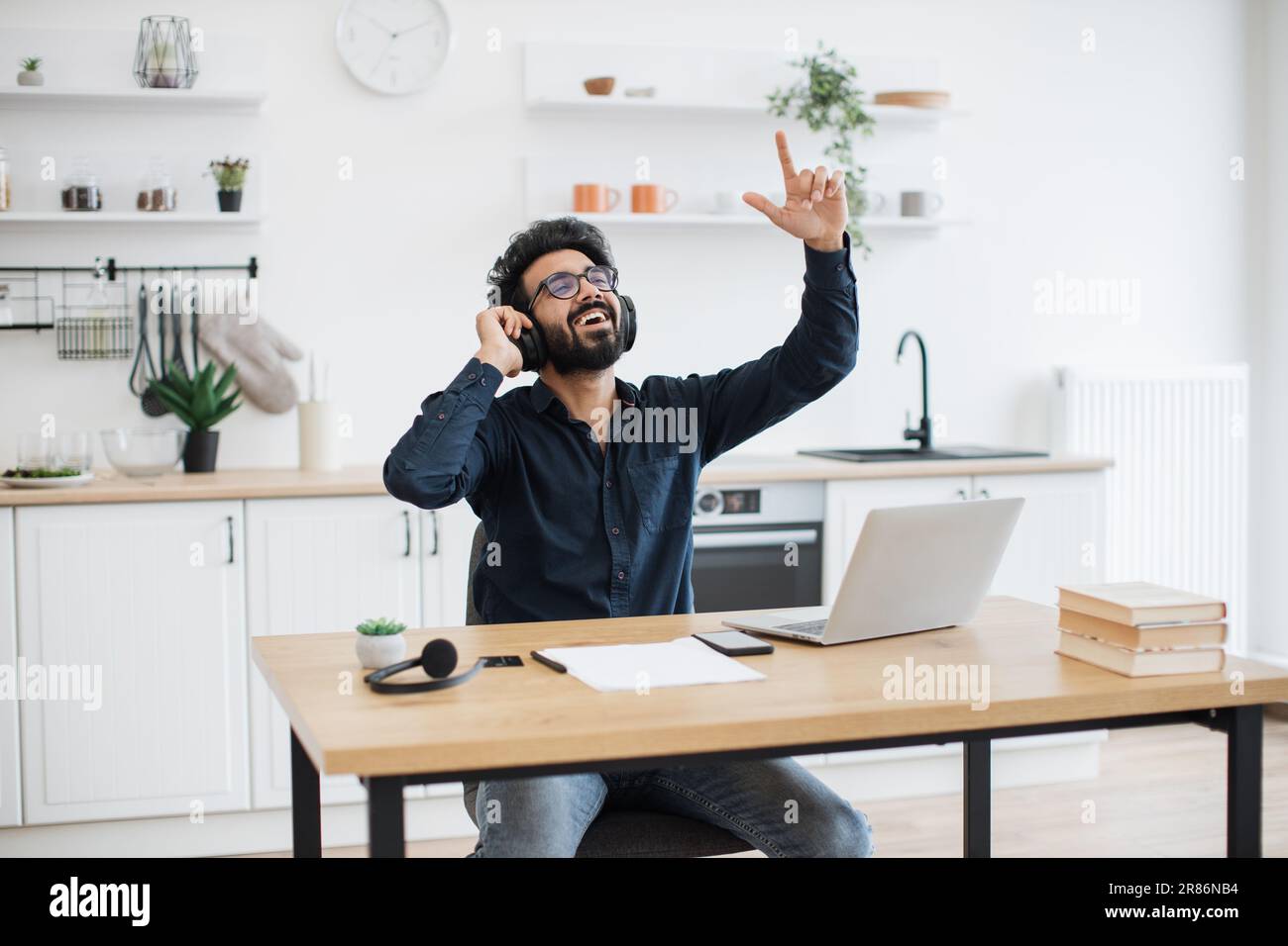 Excited young man moving hands high in air to melody while sitting with ...