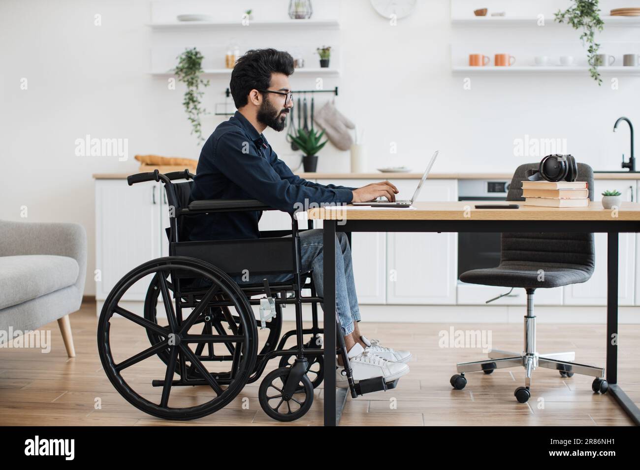 Side view portrait of indian male in wheelchair working at writing desk ...