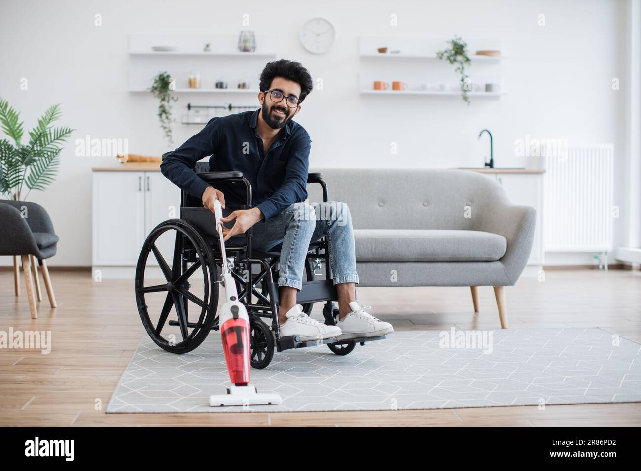 Helpful young man with disability holding cordless vacuum cleaner while ...