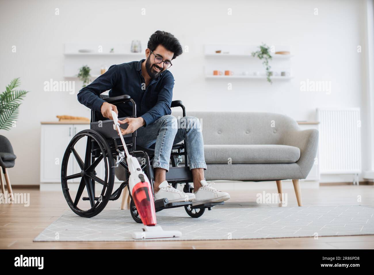 Relaxed adult person in jeans taking lightweight stick vacuum while ...