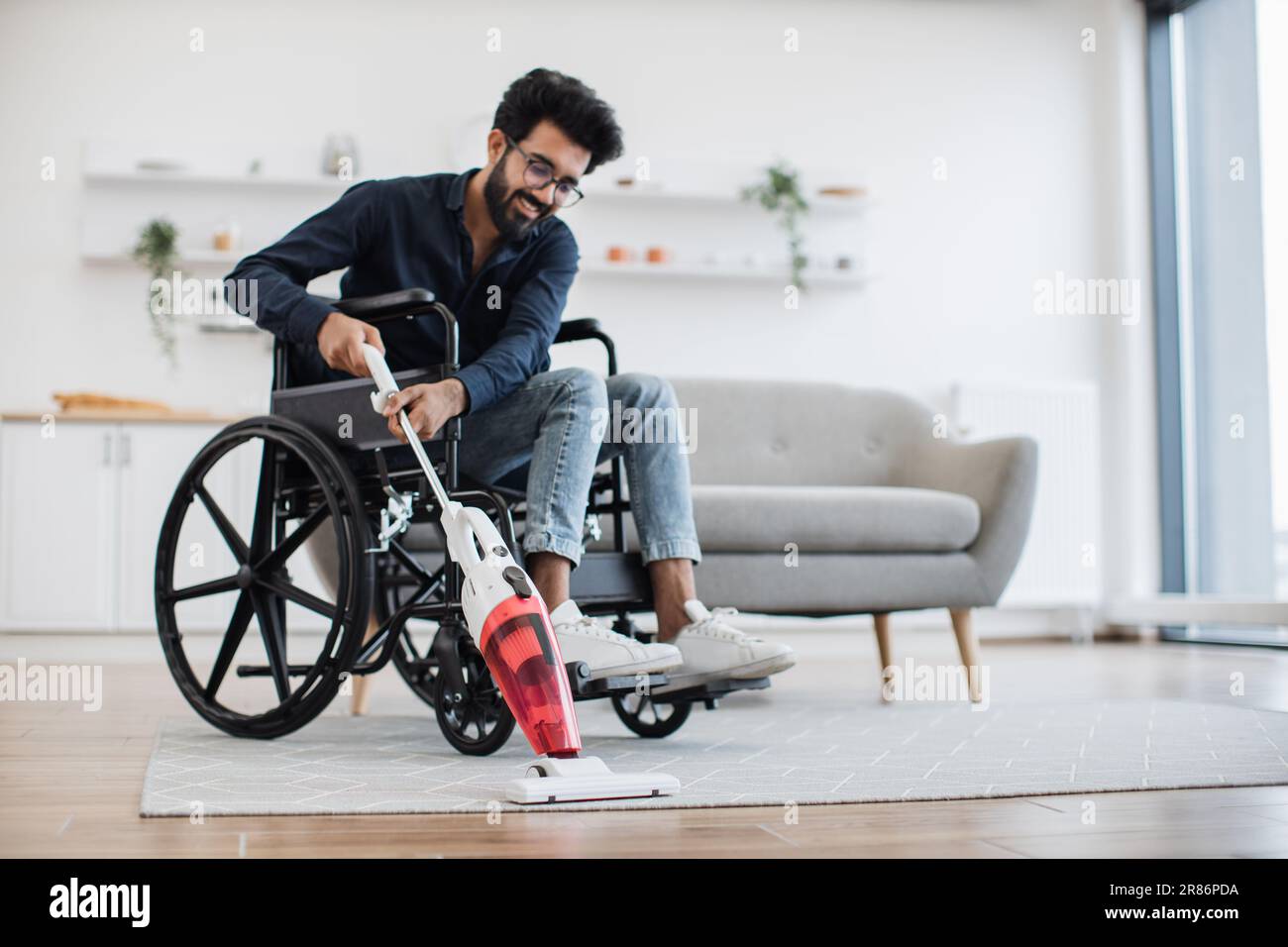 Relaxed adult person in jeans taking lightweight stick vacuum while ...