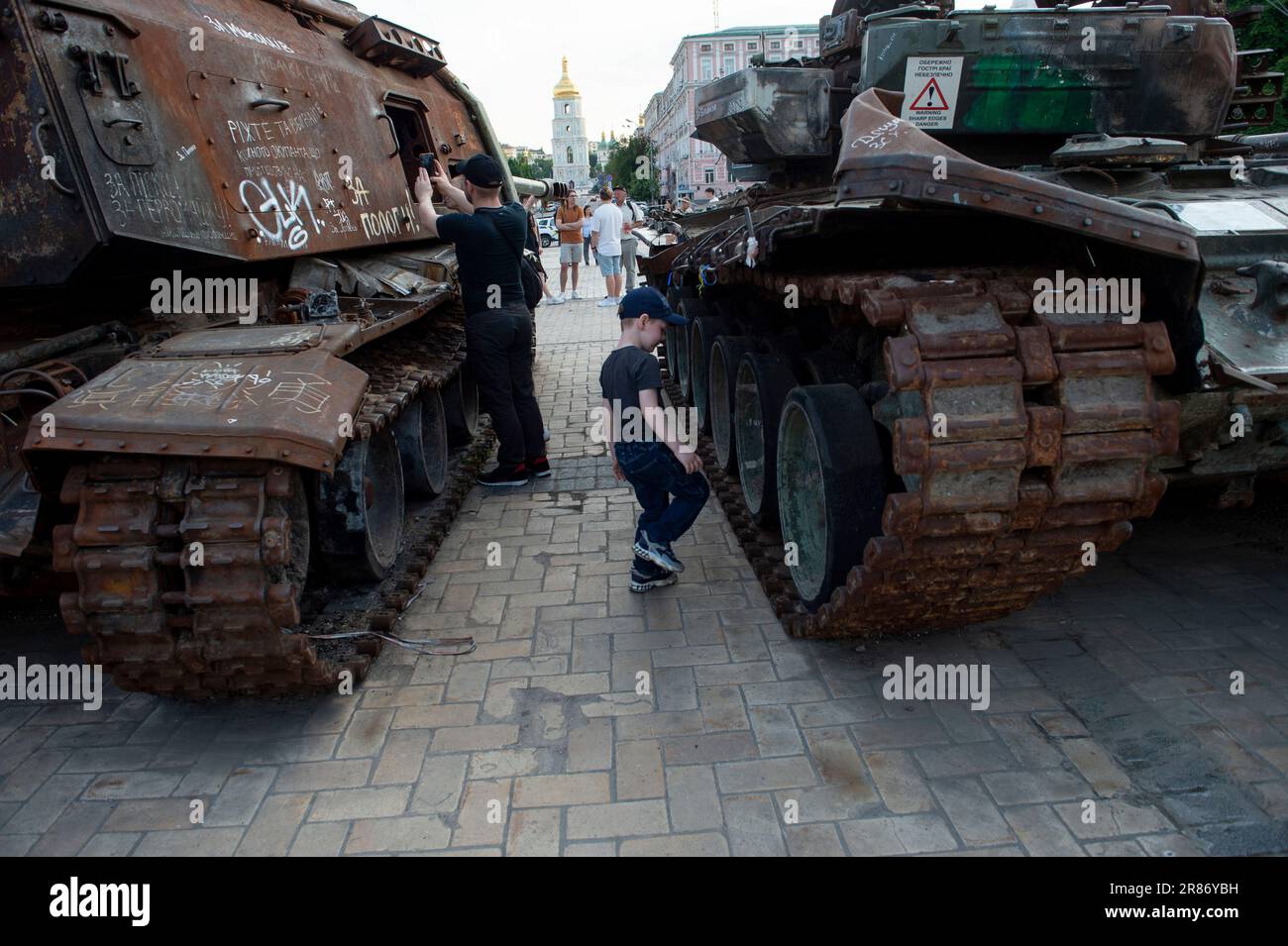 Kyiv, Ukraine. 18th June, 2023. A child kicks the treads of a Russian T ...