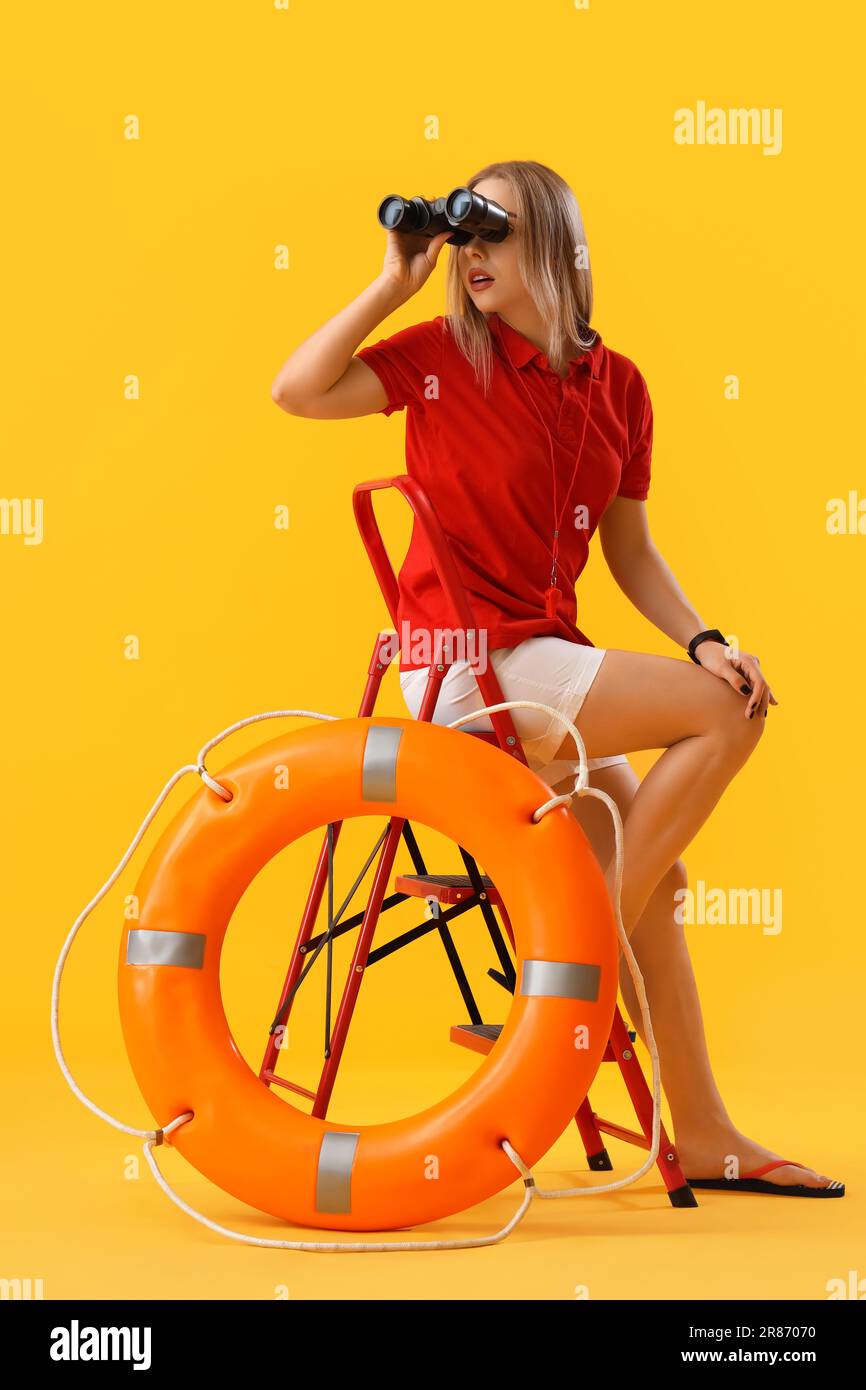 Female lifeguard with binoculars and ring buoy sitting on yellow ...