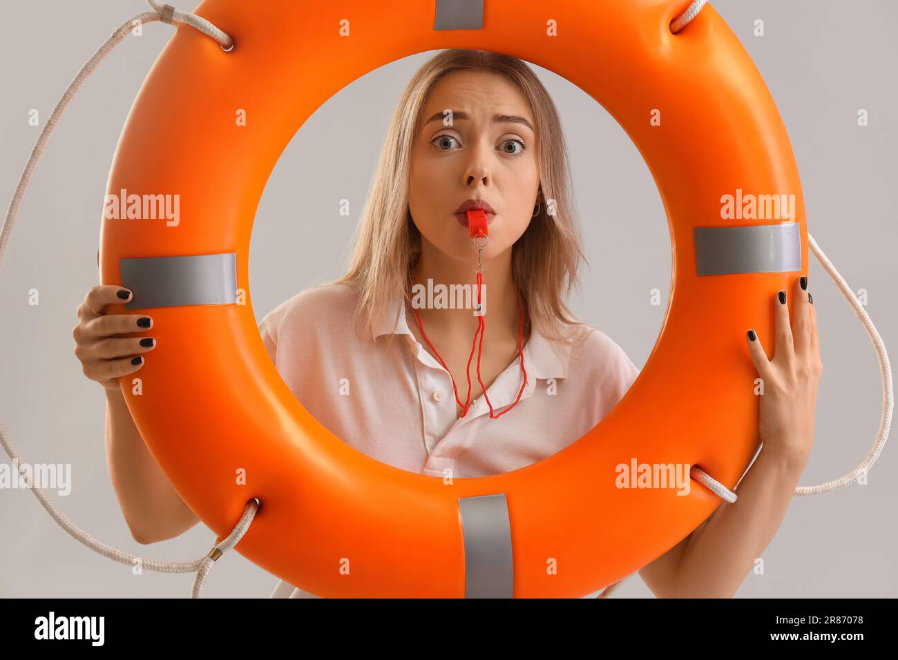 Female lifeguard with ring buoy whistling on light background Stock ...