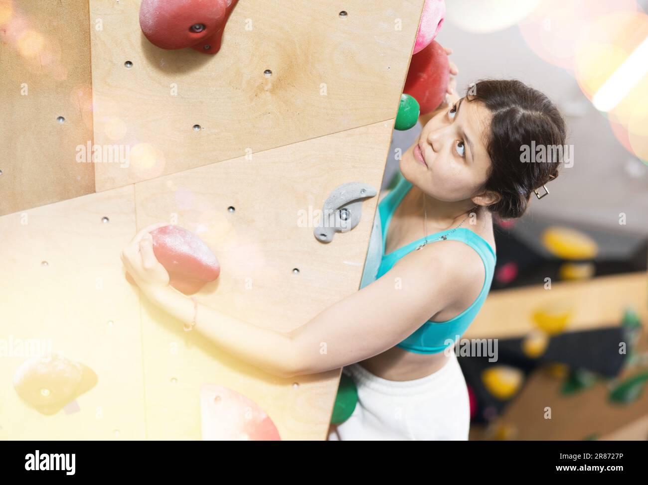 Sporty woman climbing on bouldering wall demonstrating physical strength, technical skill, and ...