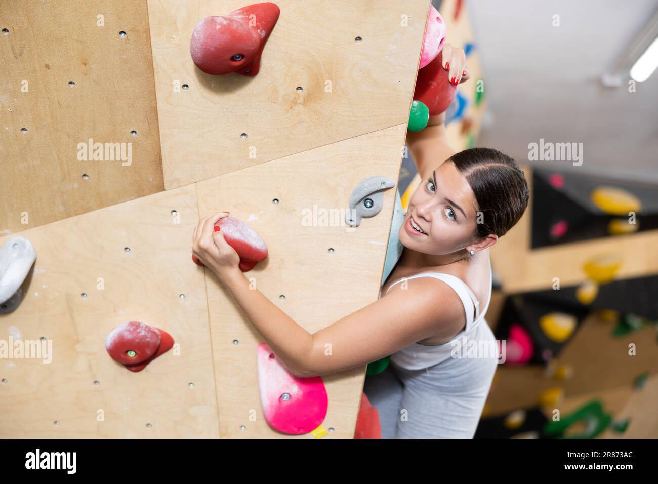Europian girl client of gym trains doing exercises on artificial wall ...