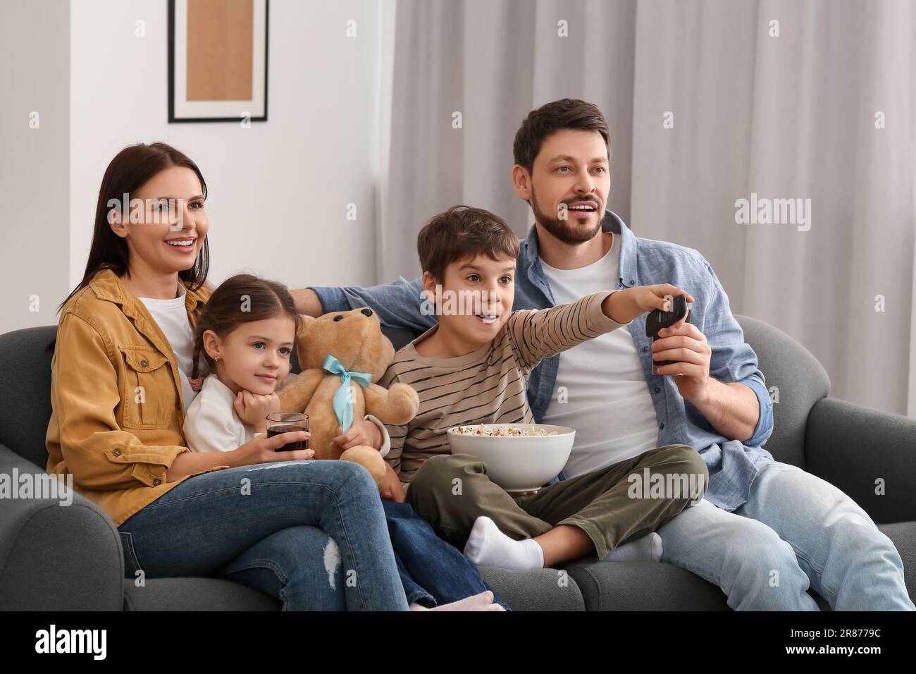 Happy family watching TV at home. Son changing channels with remote ...