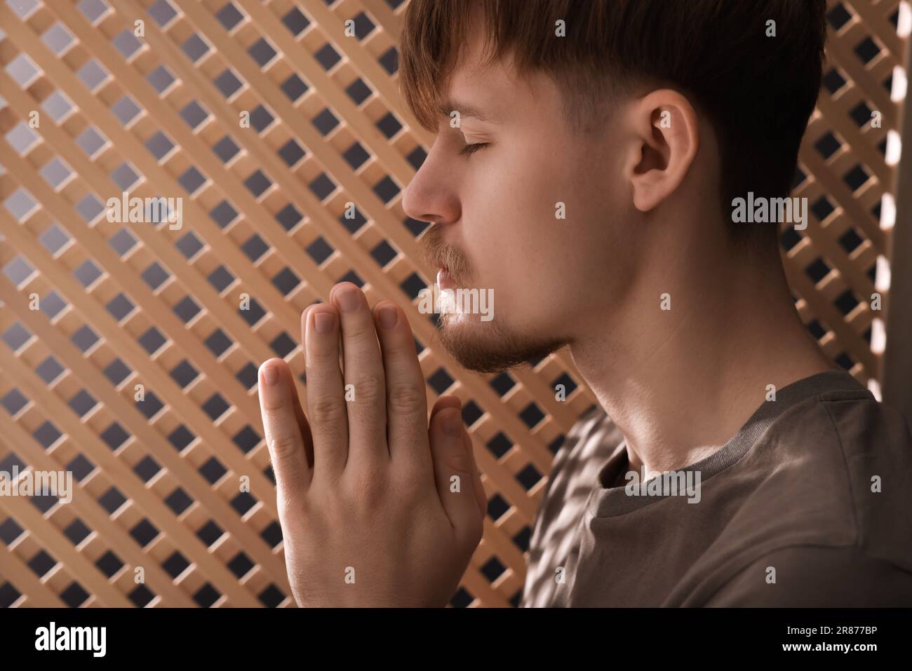 Man praying during confession near wooden window in booth, closeup ...