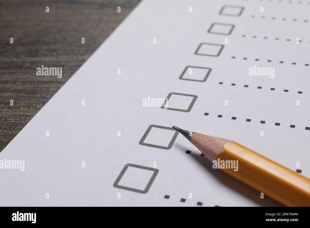 Paper sheet with checkboxes and pencil on wooden table, closeup ...