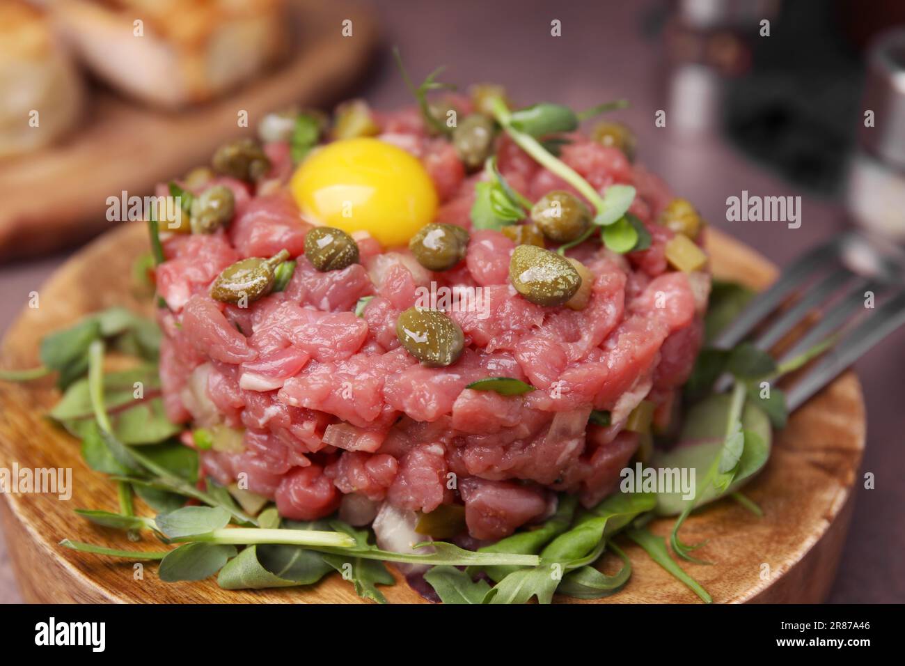 Tasty beef steak tartare served yolk, capers and microgreens on serving ...