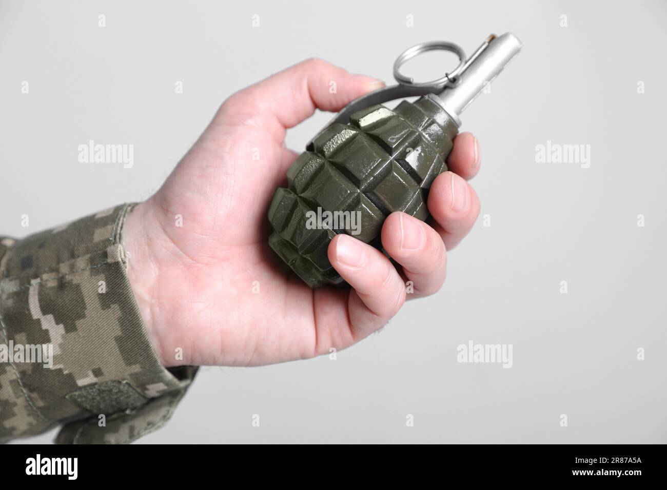 Soldier holding hand grenade on light grey background, closeup ...