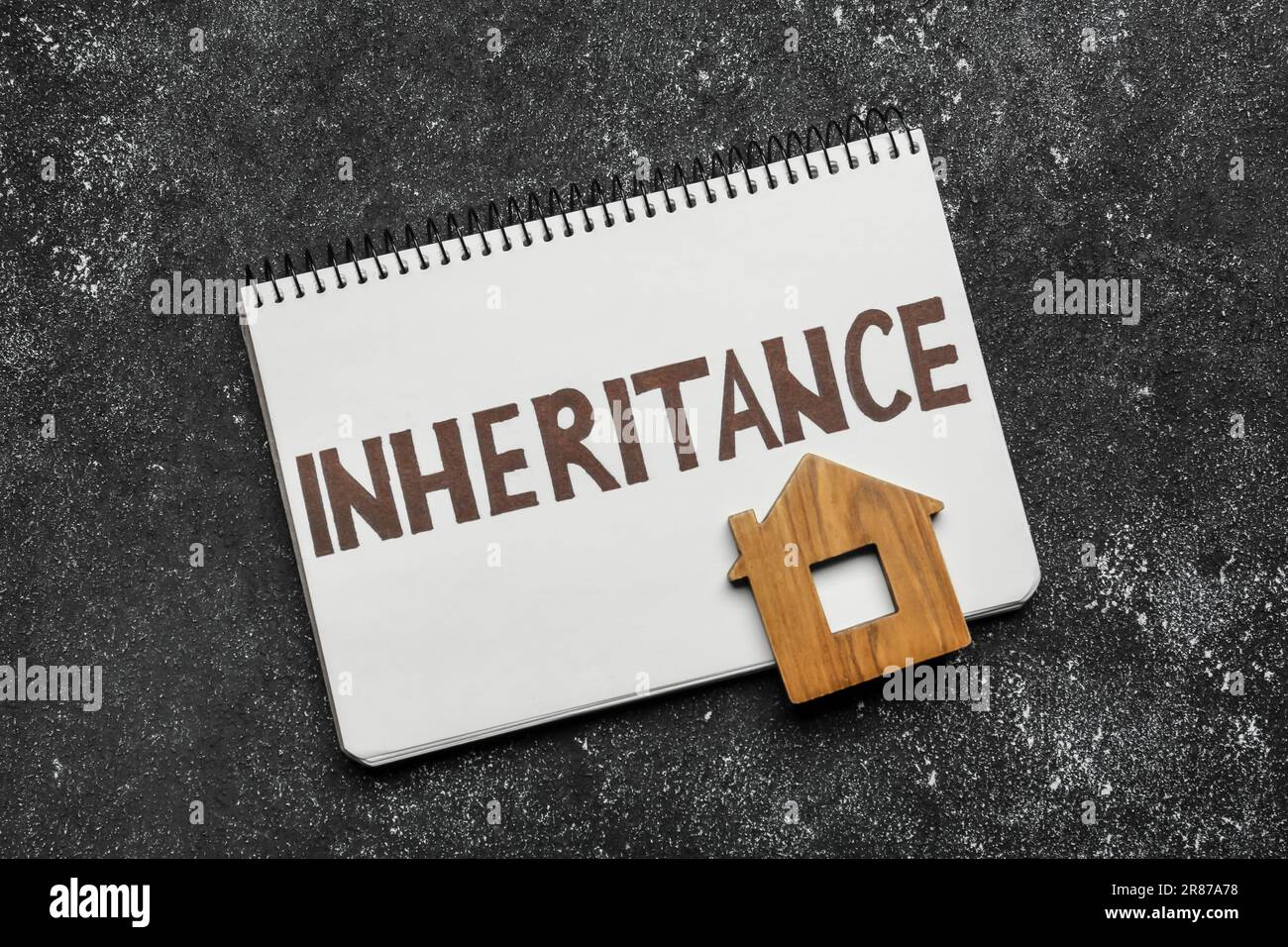 Notebook with word Inheritance and model of house on black background ...