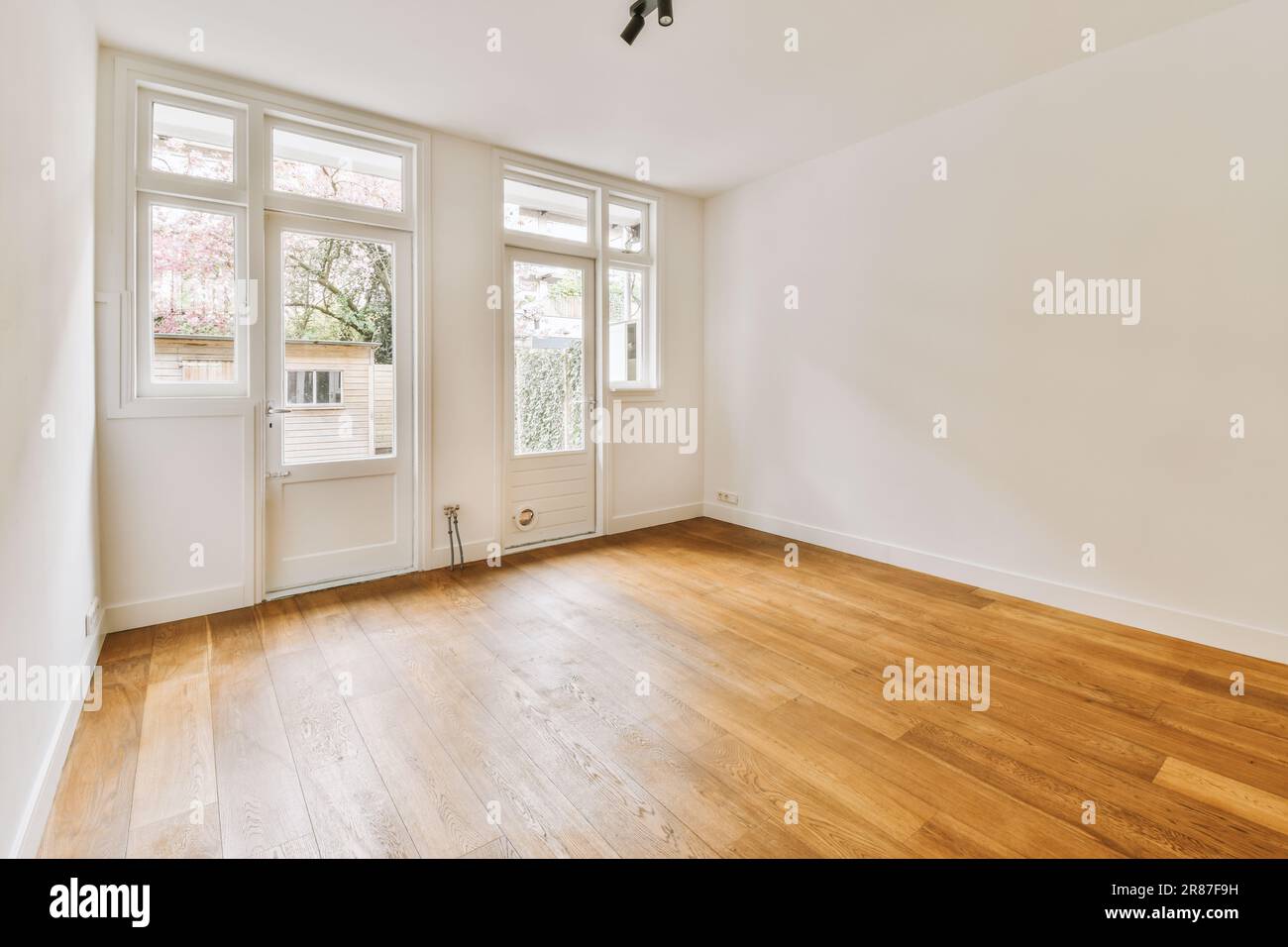 an empty living room with wood flooring and two windows looking out ...