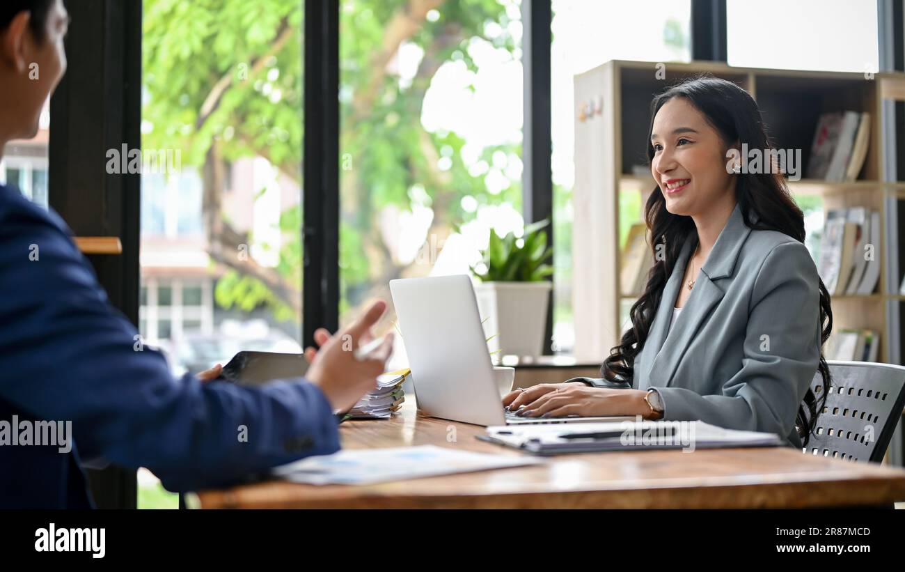 A beautiful millennial Asian businesswoman is listening to her male ...