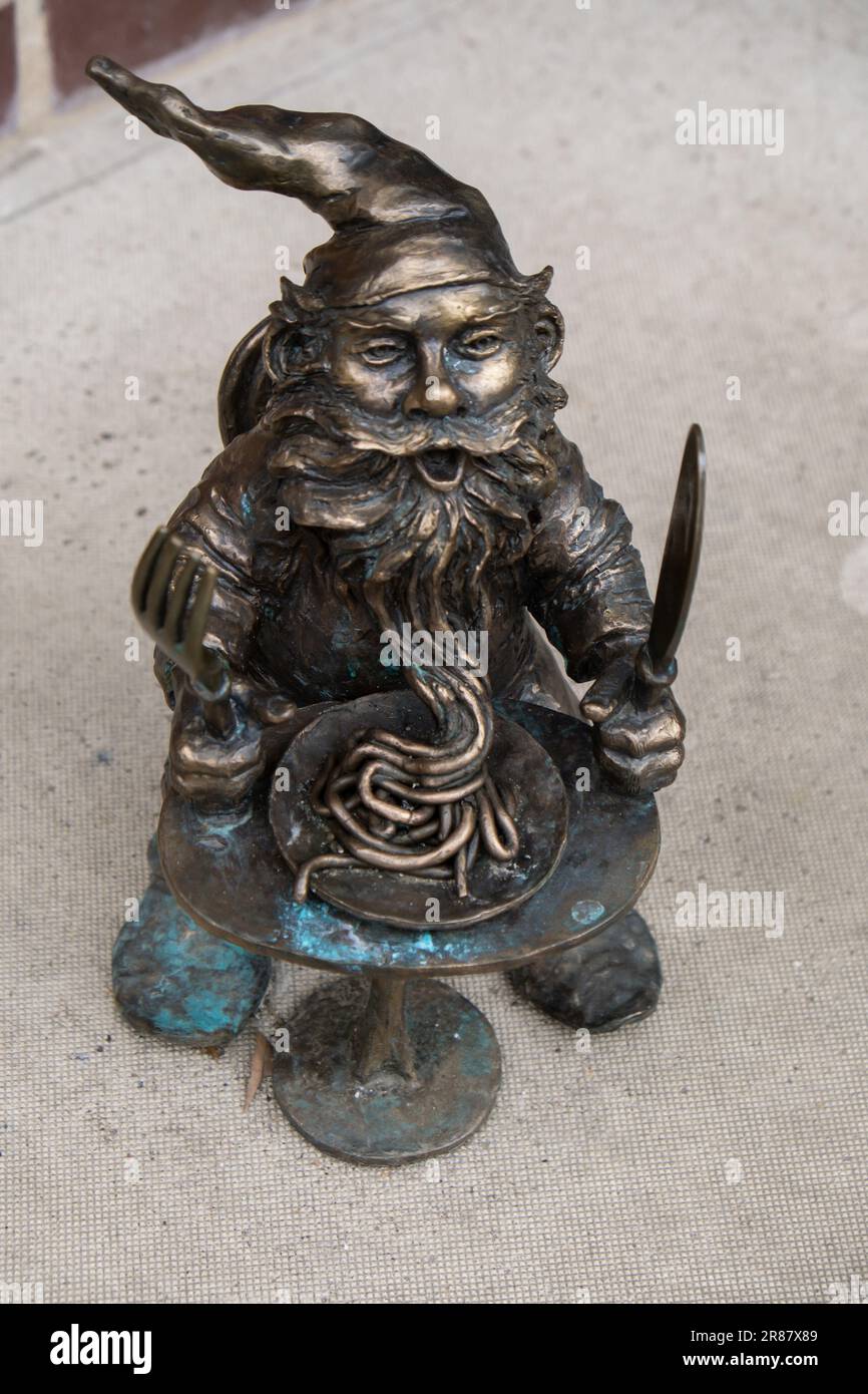 Dwarf eats pasta near restaurant. Small bronze figures of gnomes on the ...