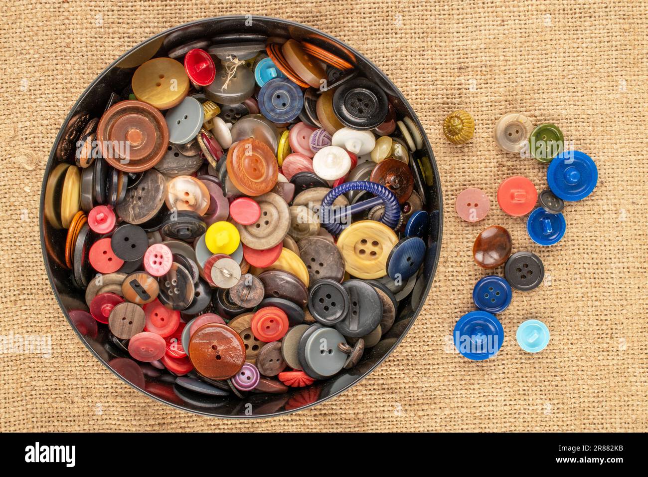 Many buttons in a plastic container on a jute canvas, macro, top view ...