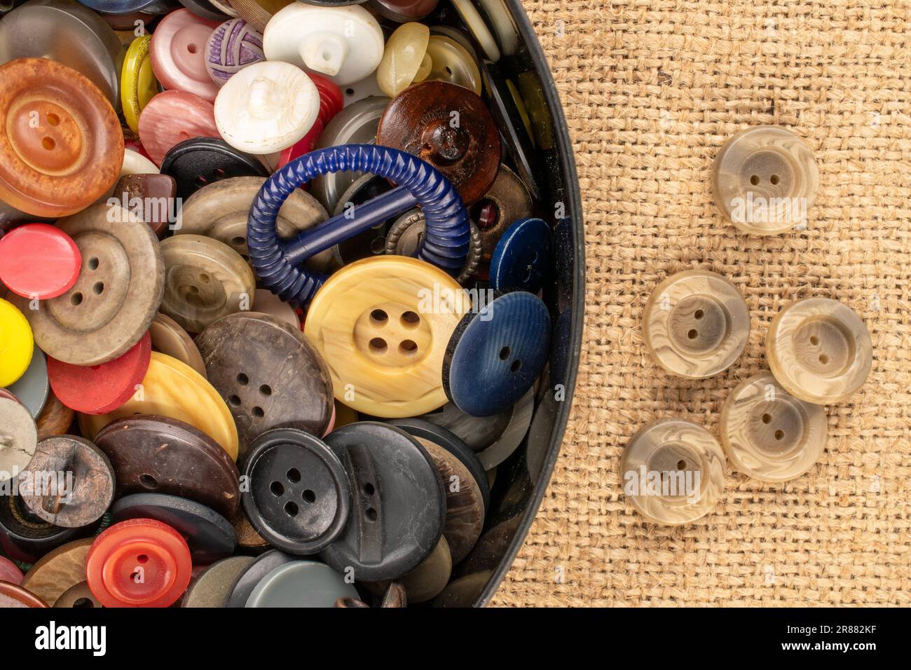 Many buttons in a plastic container on a jute canvas, macro, top view ...