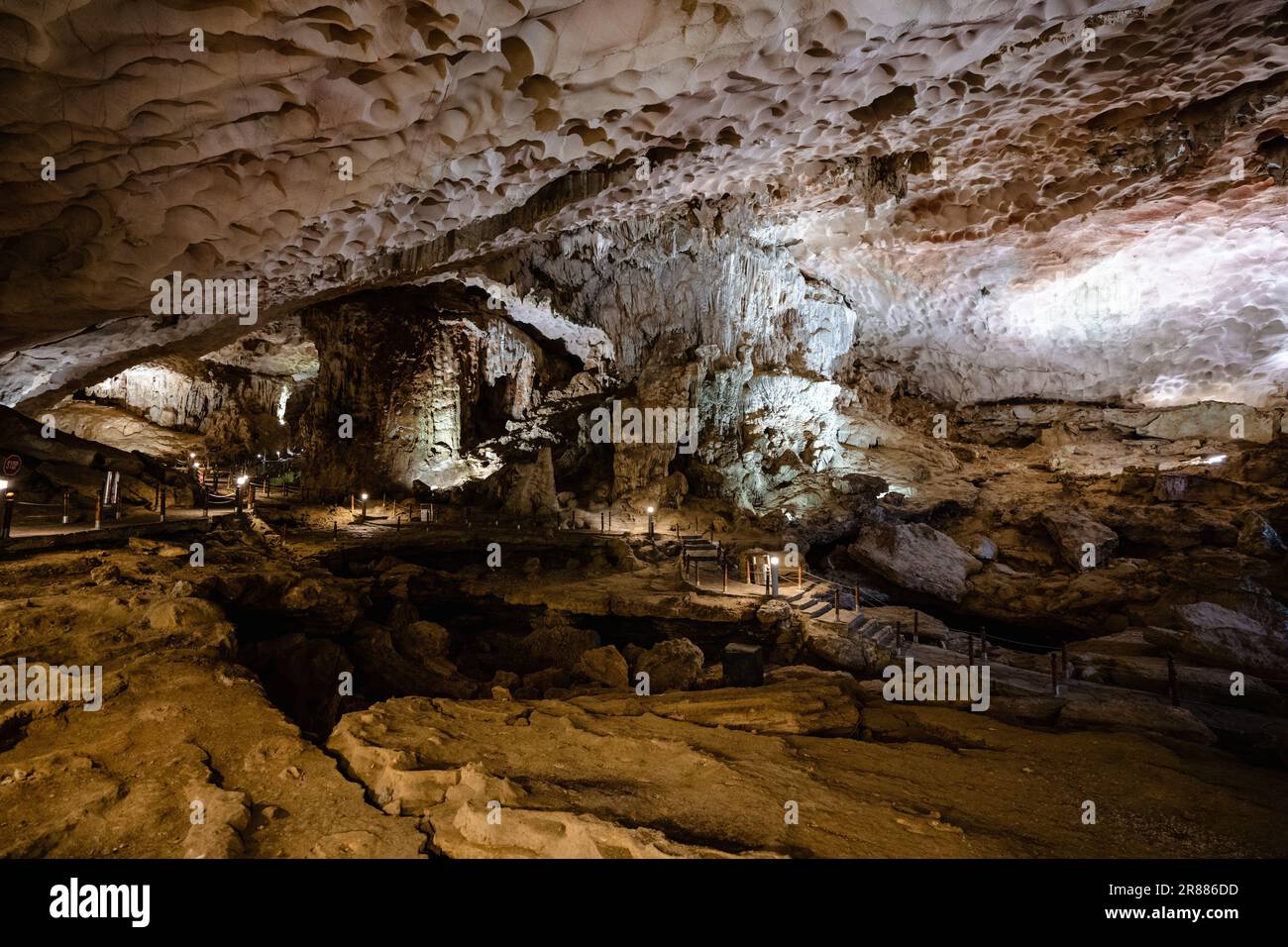 An underground cave illuminated by warm white lighting with a walkway ...