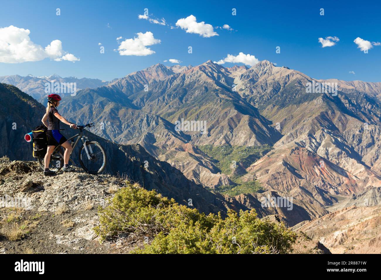 Bicycle traveler with loaded bike standing at cliff and enjoying view of mountains. Pontic ...