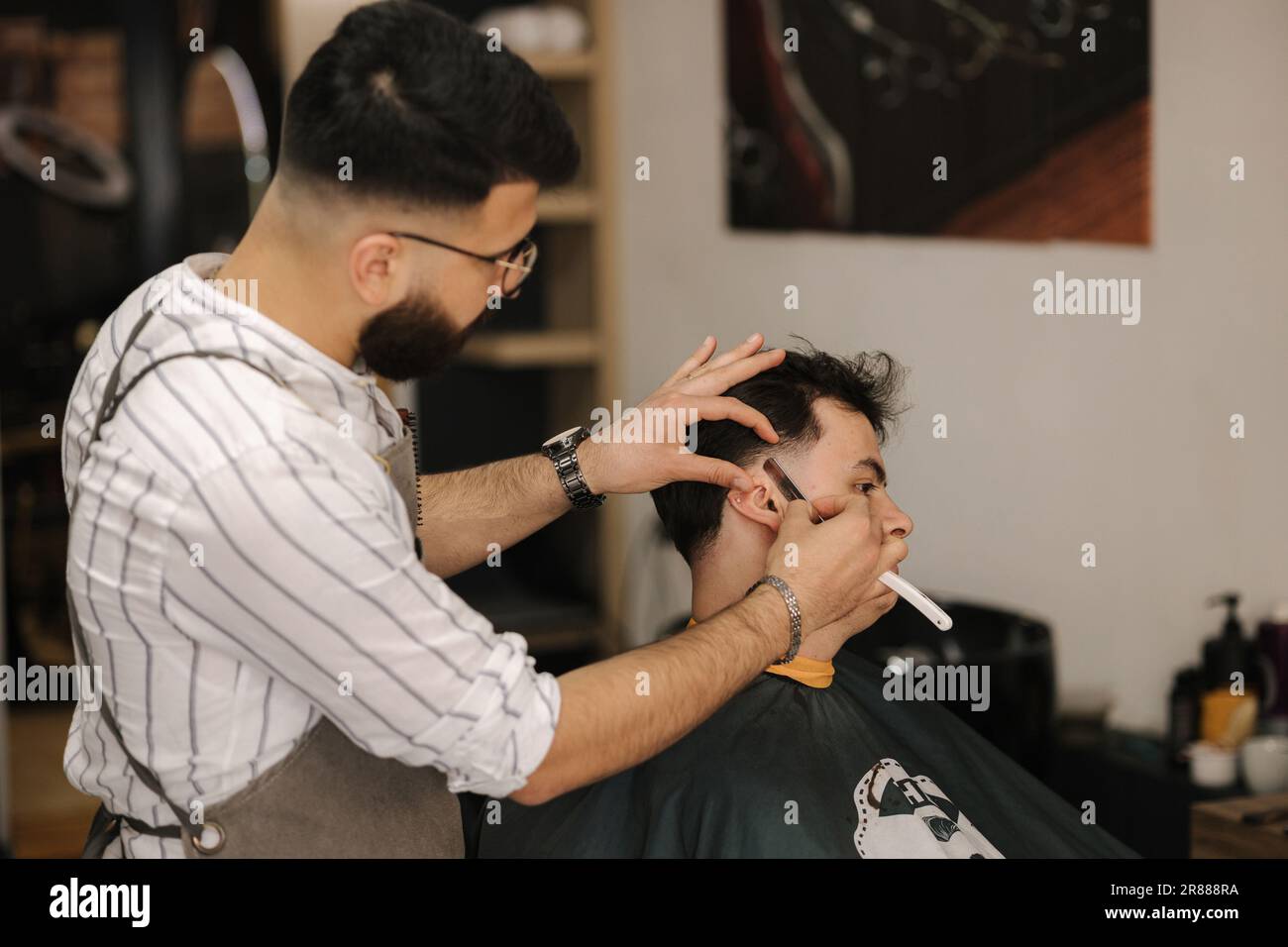Side view of barber using sharp blade for shaving. Handsome customer ...