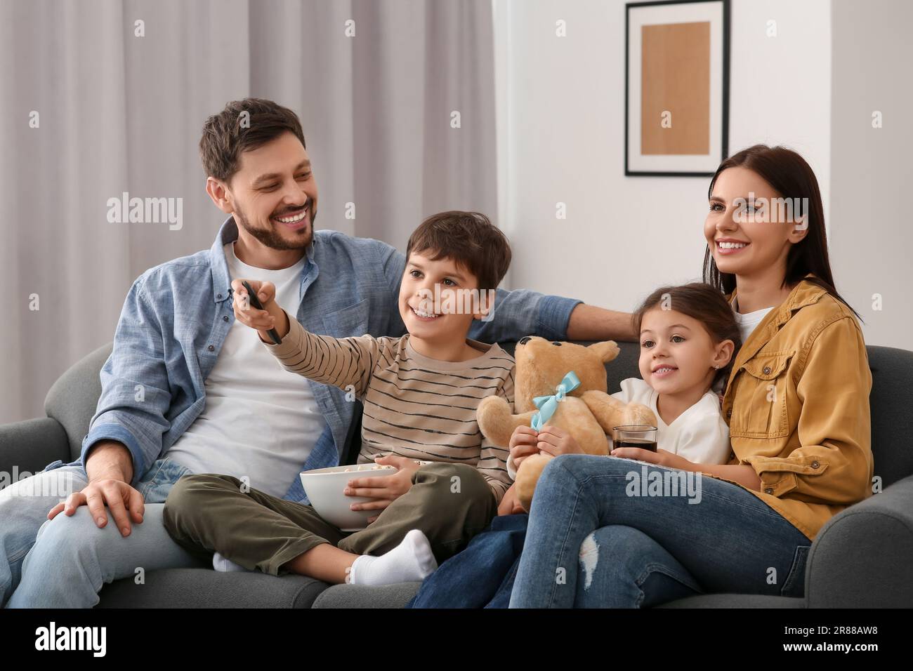 Happy family watching TV at home. Son changing channels with remote ...