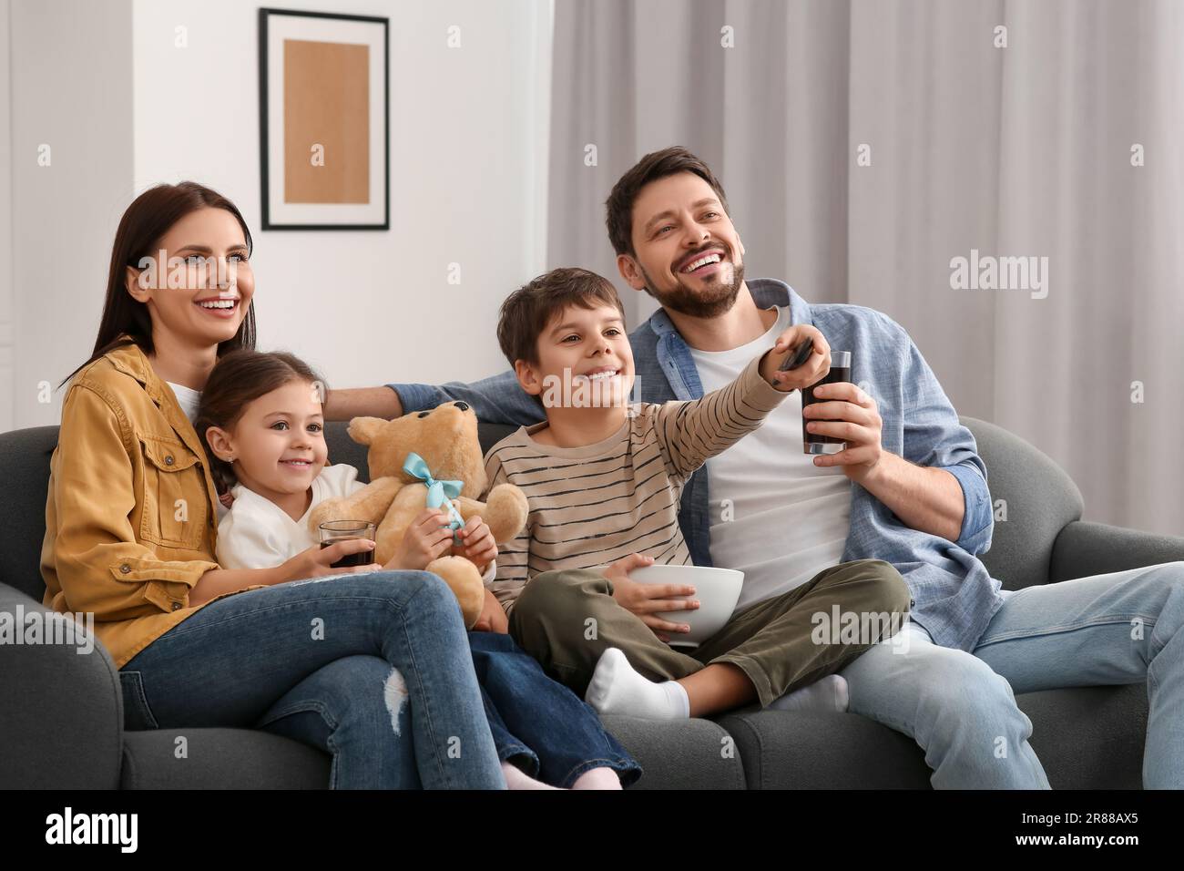 Happy family watching TV at home. Son changing channels with remote ...