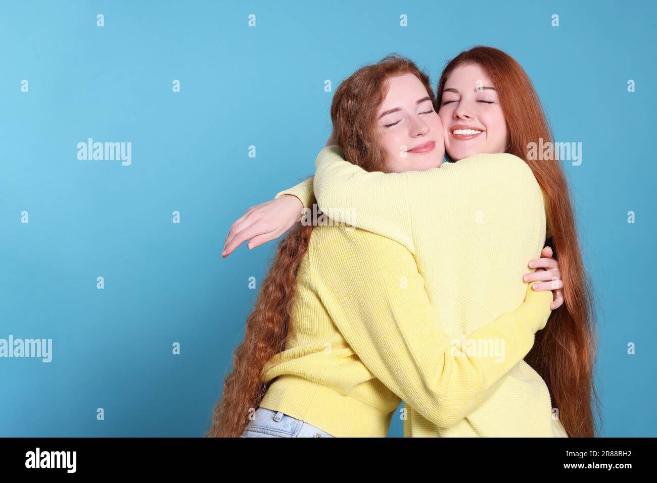 Portrait of beautiful young redhead sisters on light blue background ...