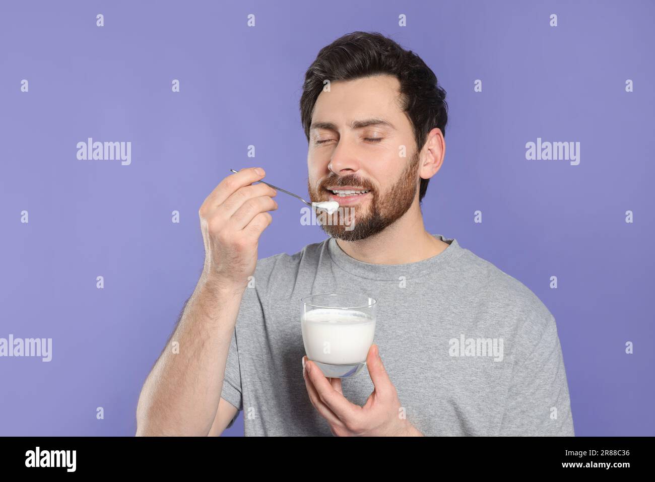Handsome man eating delicious yogurt on violet background Stock Photo ...