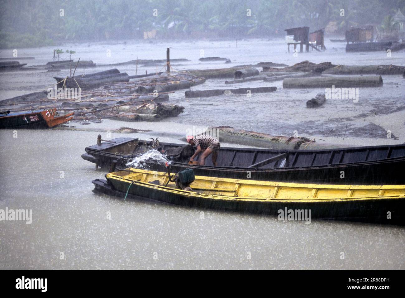 A boatmen tries to remove the water from his boat as the rain pours ...