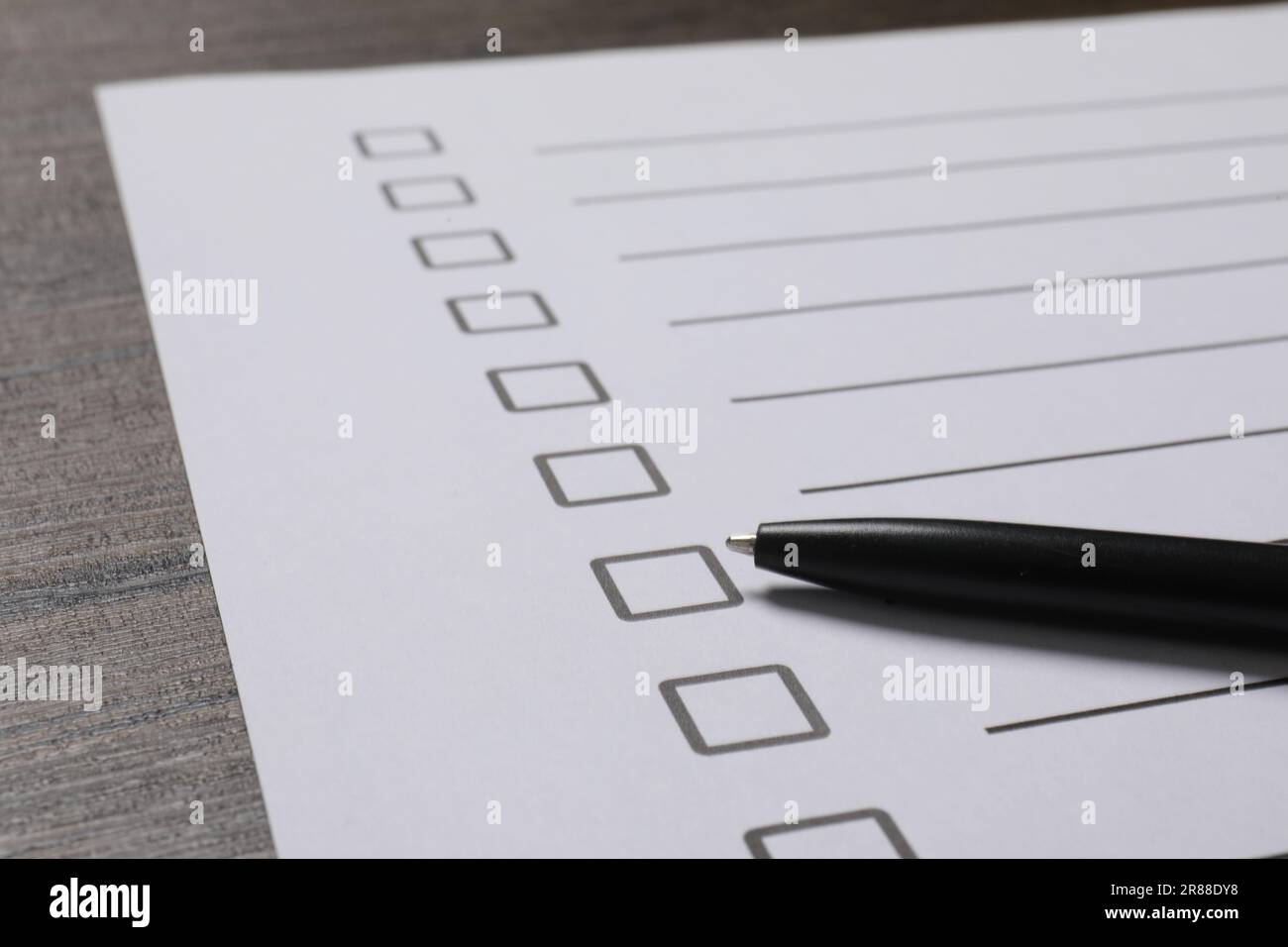 Paper sheet with checkboxes and pen on wooden table, closeup. Checklist ...