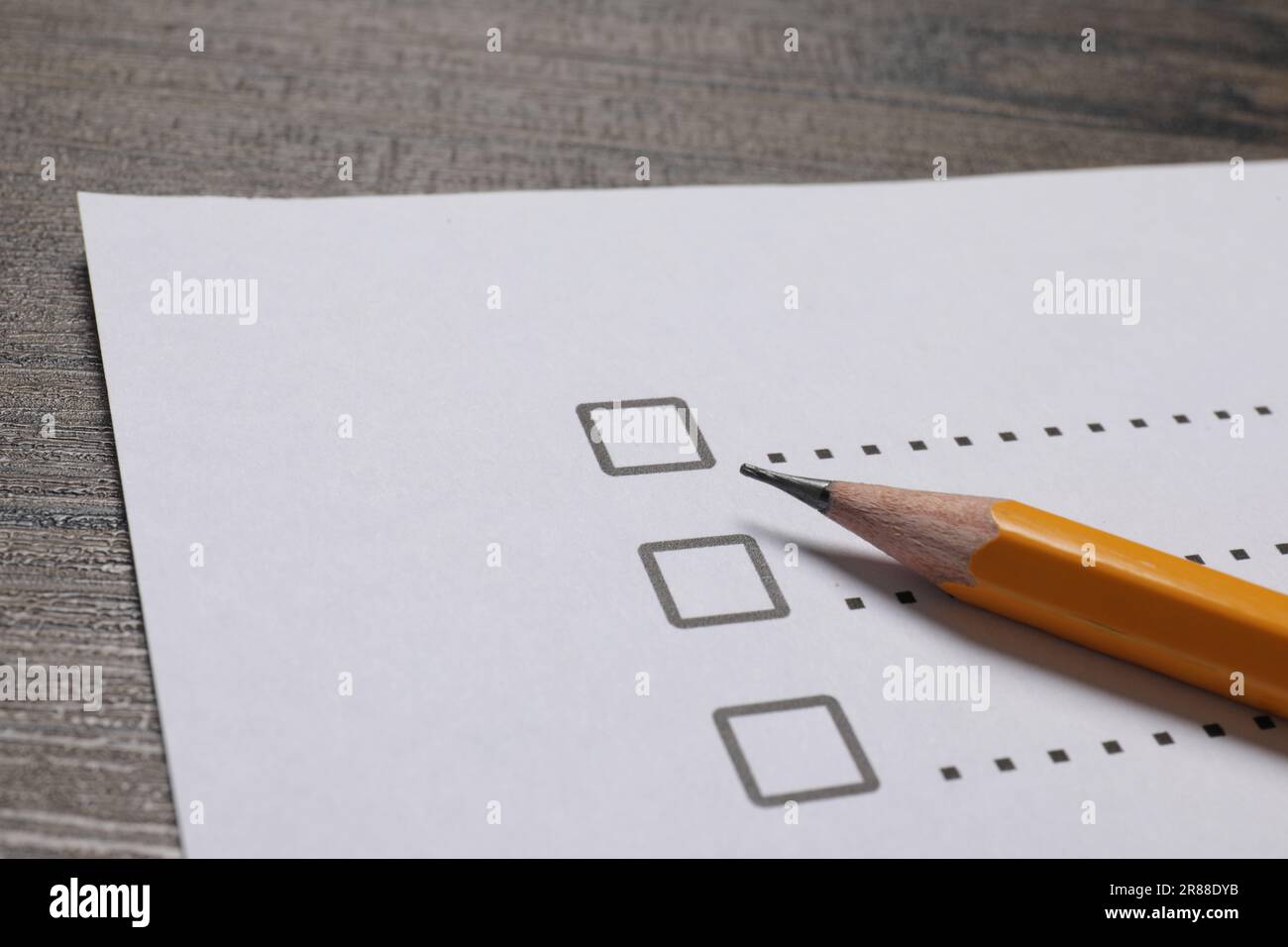 Paper sheet with checkboxes and pencil on wooden table, closeup ...