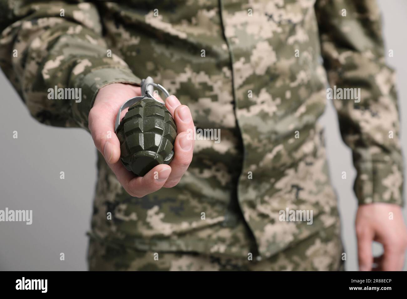 Soldier holding hand grenade on light grey background, closeup ...