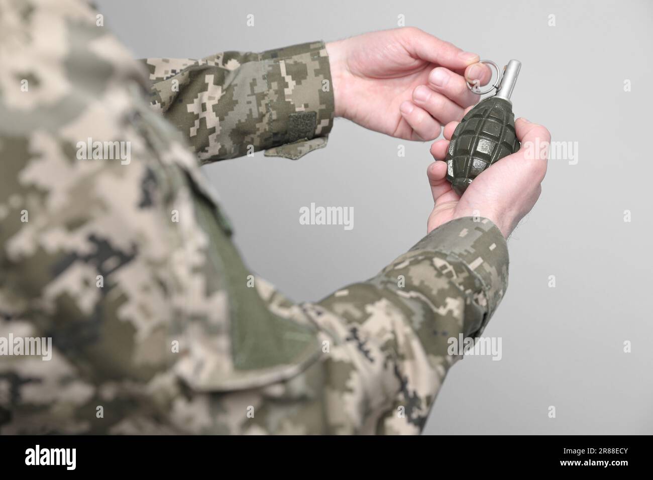 Soldier pulling safety pin out of hand grenade on light grey background ...