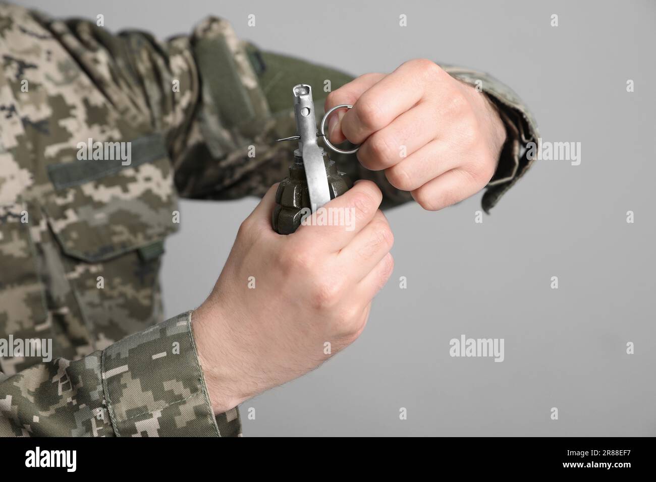 Soldier pulling safety pin out of hand grenade on light grey background ...