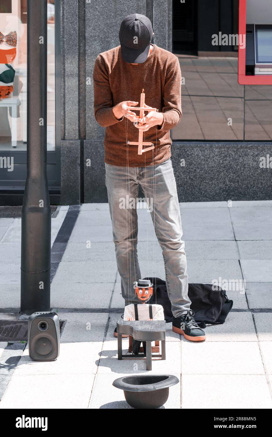 A street performer manipulating a wooden puppet playing the piano ...